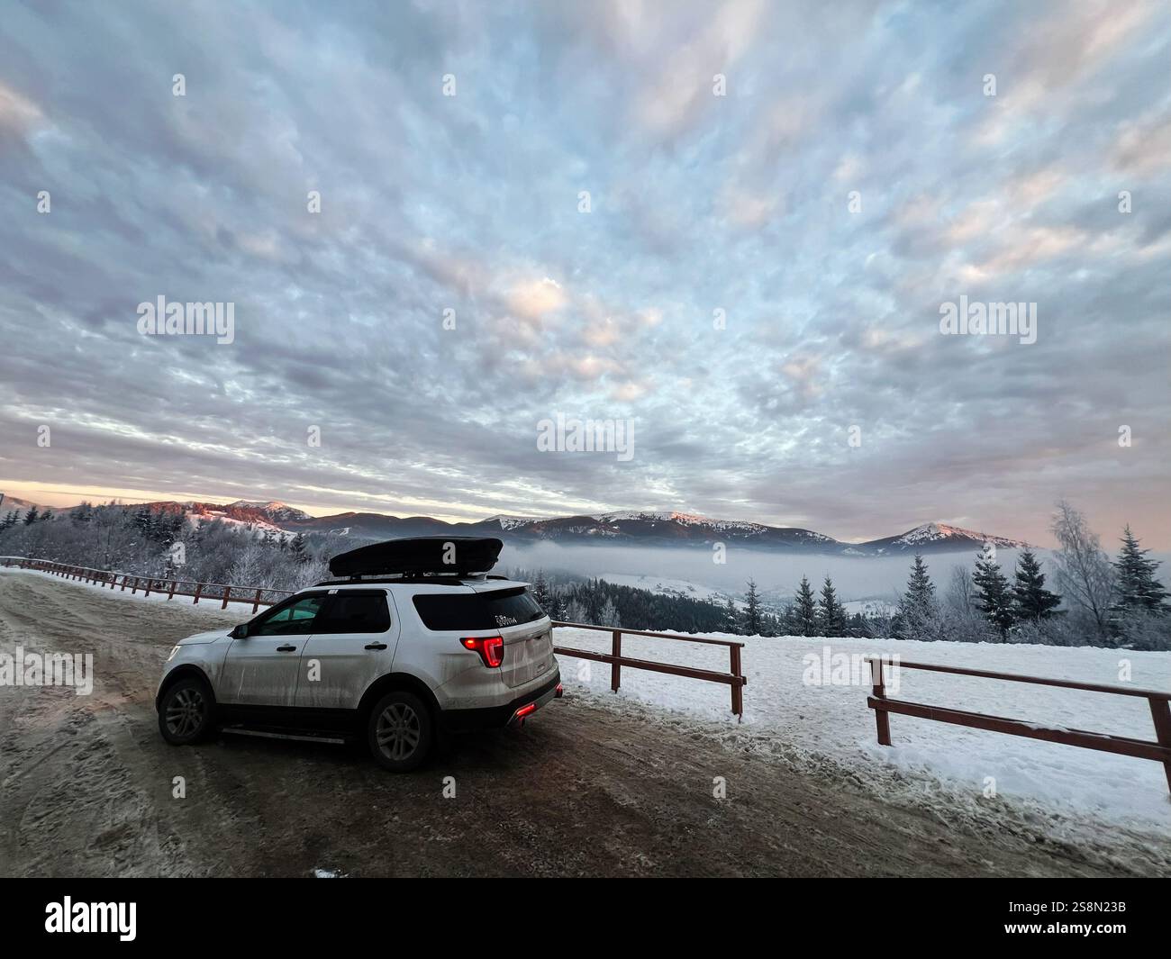 An SUV is parked in a snowy mountain area on a clear sunrise morning ...