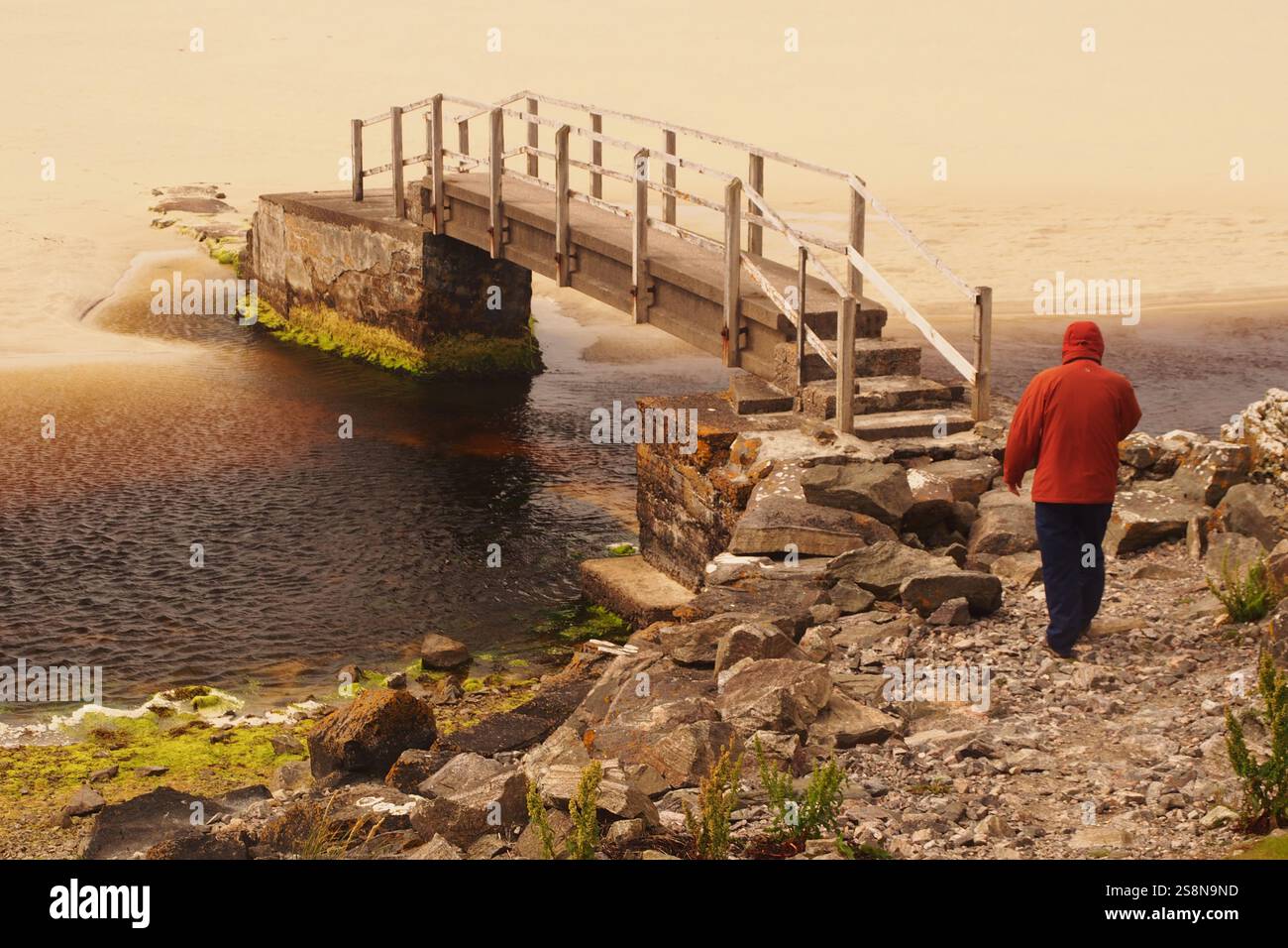 A man crossing the wooden footbridge connecting Uig beach with the ...