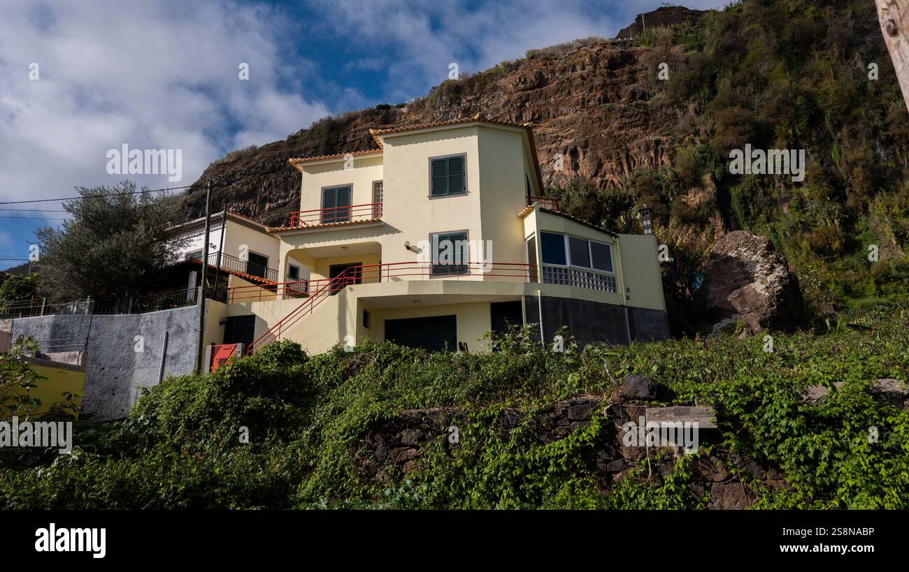 A modern hillside house with a bright yellow facade, large windows, and ...
