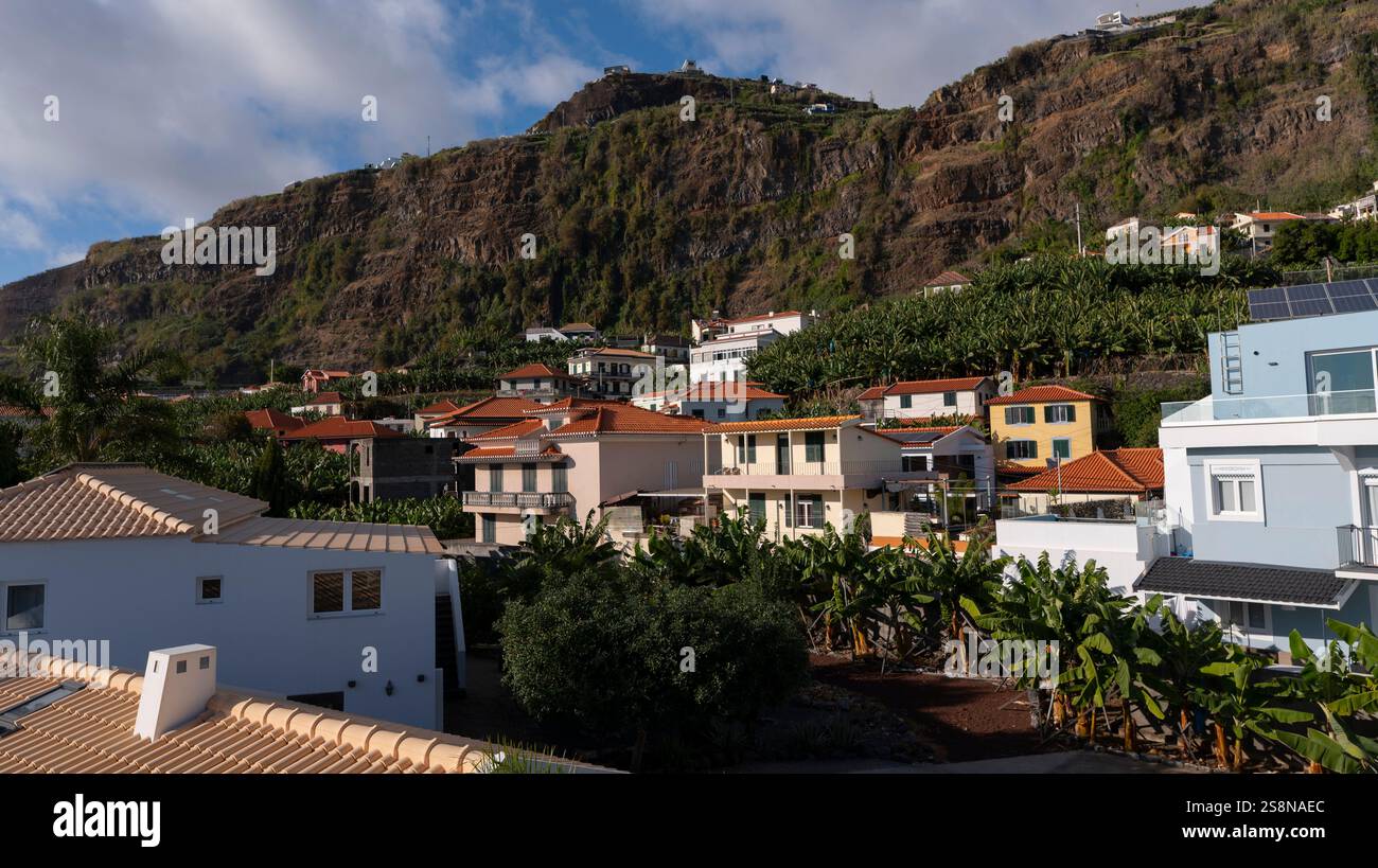 A picturesque hillside village with colorful houses, banana plantations, and a dramatic rocky ...