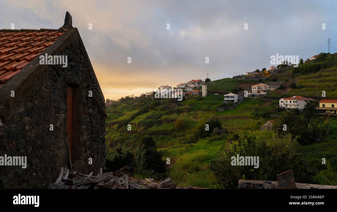 A scenic hillside village at sunset, featuring terraced green fields ...