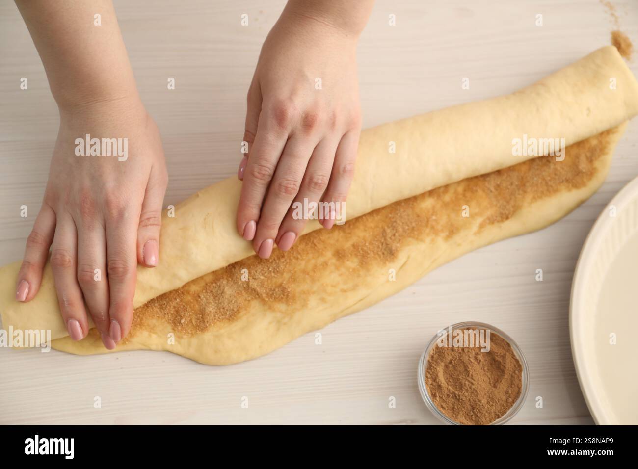 Making cinnamon rolls. Woman shaping dough at white wooden table, top ...