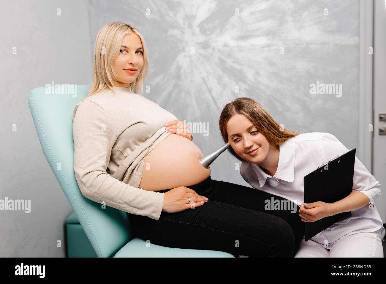 A gynecologist leans a stethoscope to a pregnant woman's belly and ...