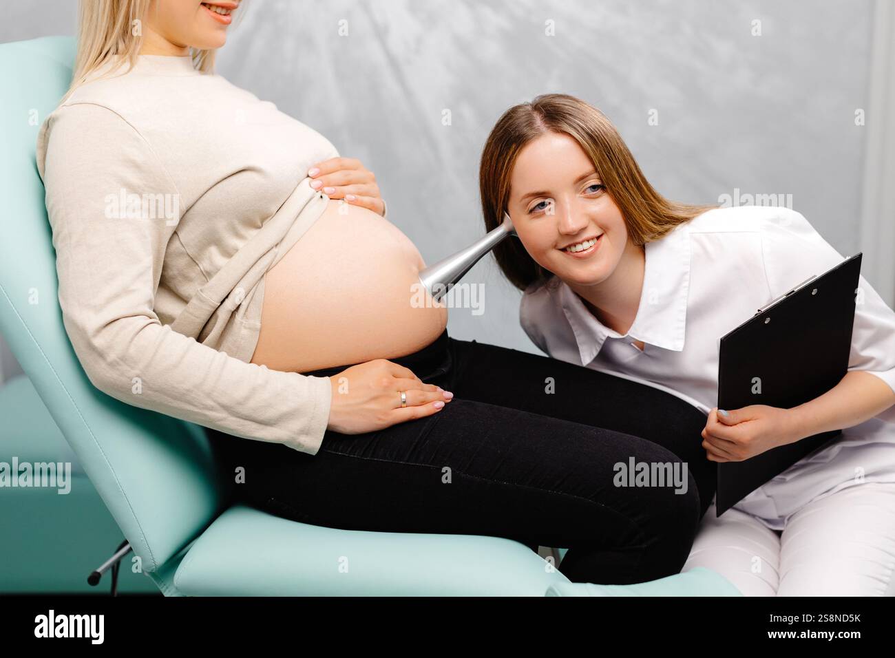 A gynecologist leans a stethoscope to a pregnant woman's belly and ...
