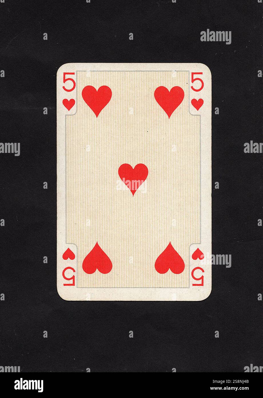 An antique five of hearts playing card isolated on a black background ...