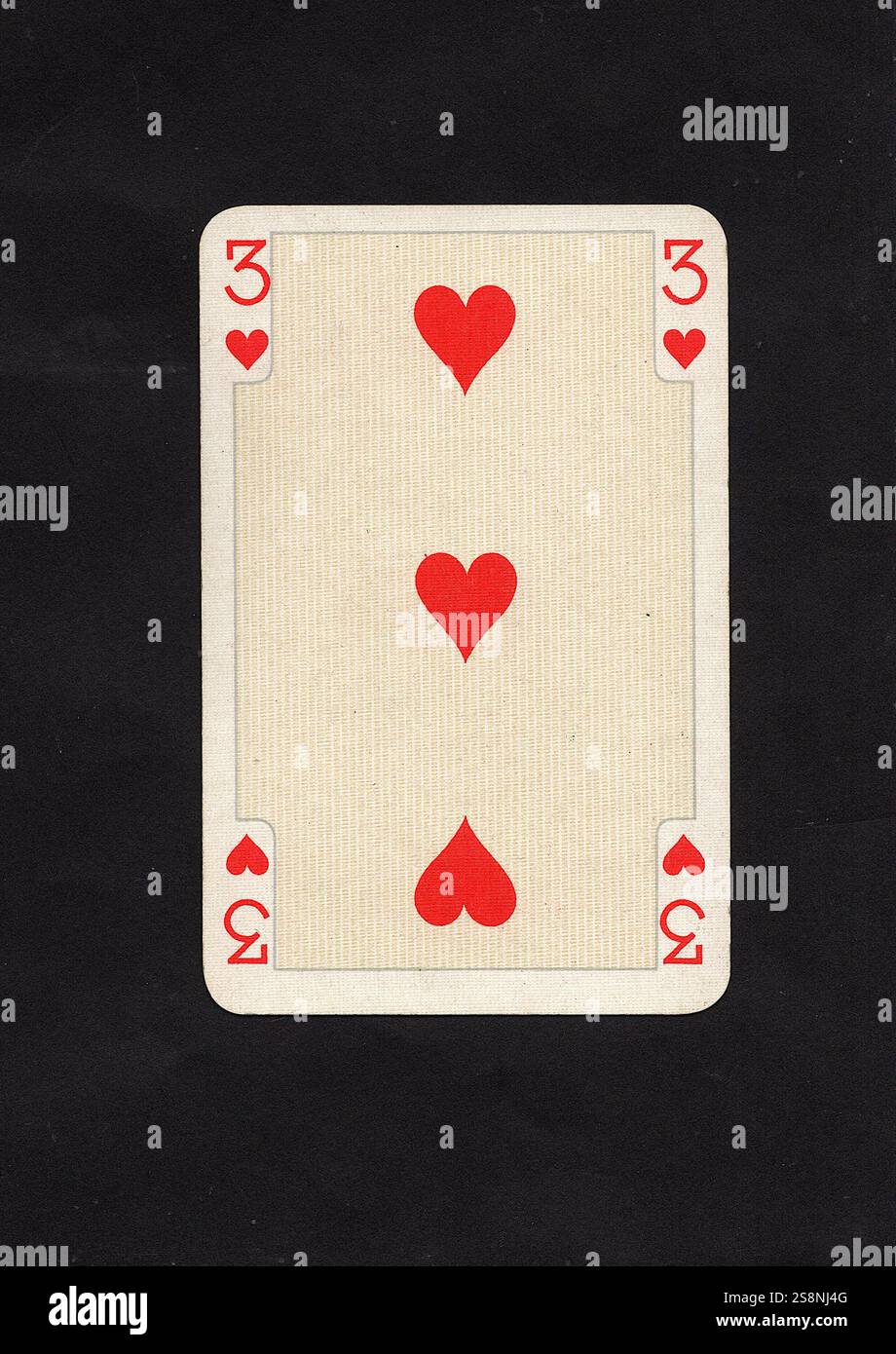 An antique three of hearts playing card isolated on a black background ...