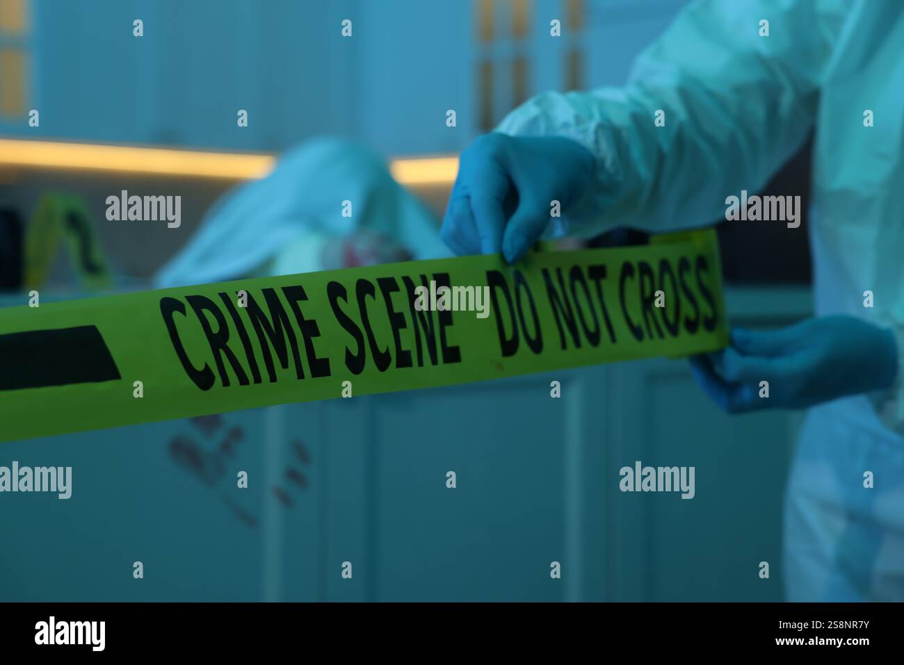 Forensic expert blocking way to crime scene with yellow tape indoors ...