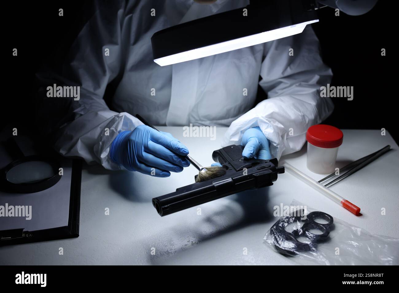 Forensic expert taking fingerprints with brush from gun at table ...