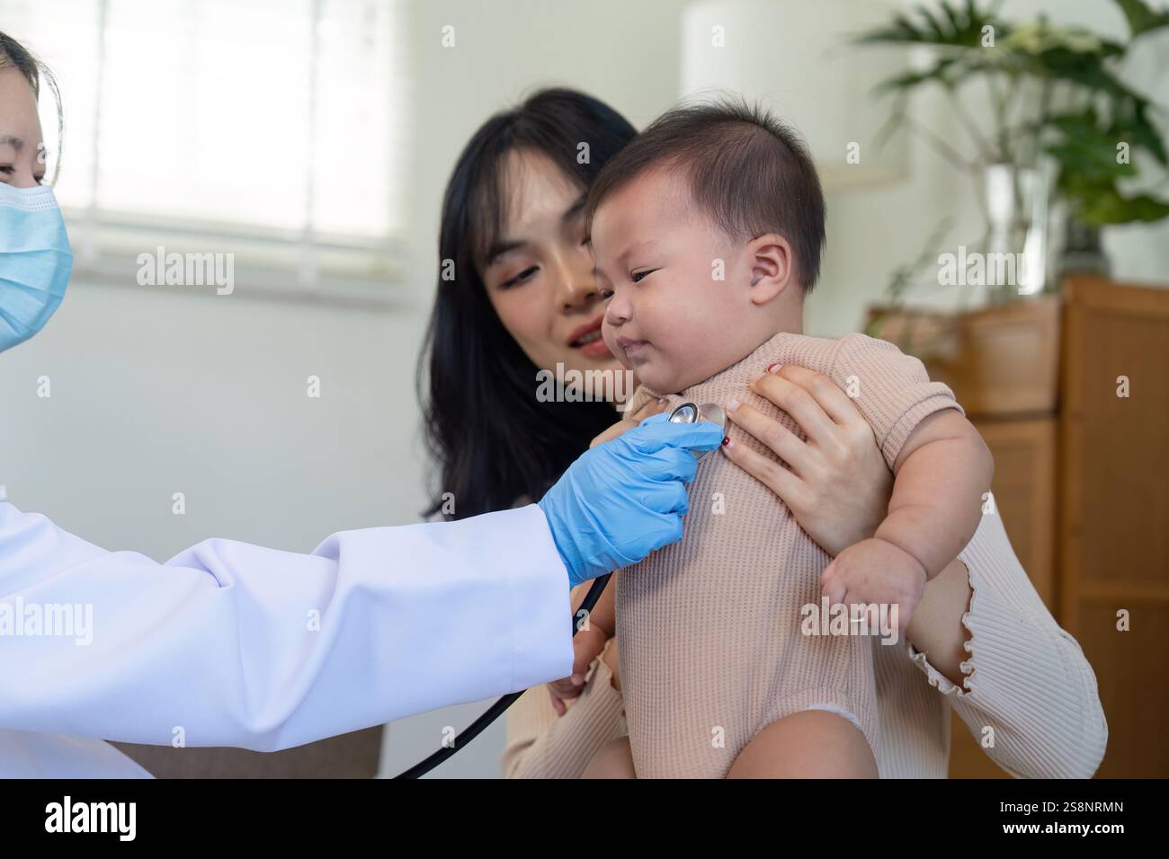 Pediatrician checking baby's heartbeat as concerned mother looks on ...