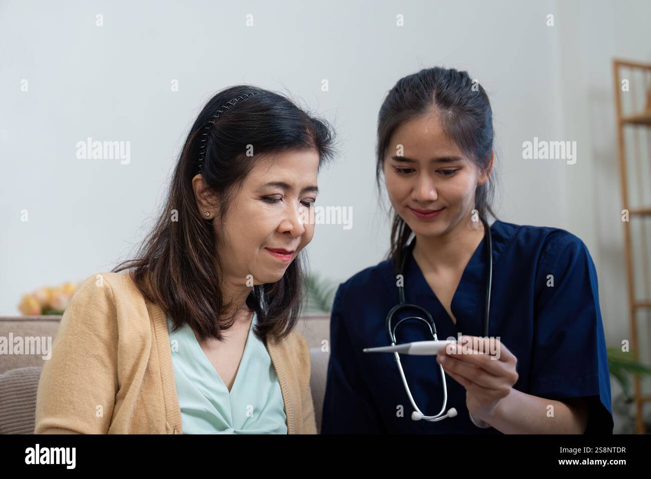 Caregiver checking thermometer reading for elderly patient, monitoring ...