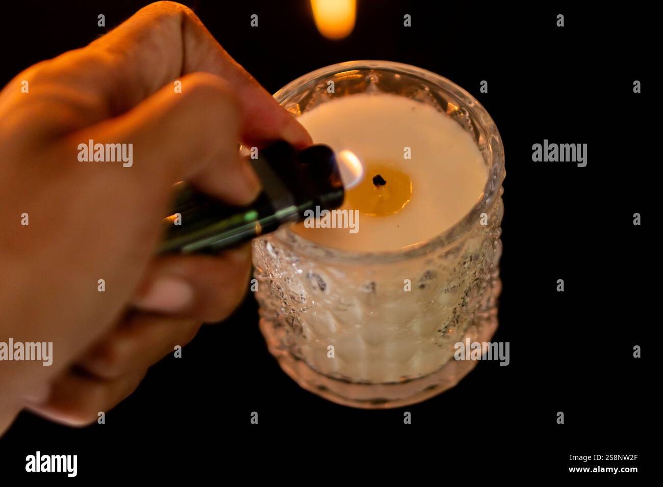 A hand holding a lighter to ignite a candle in a glass holder. The ...
