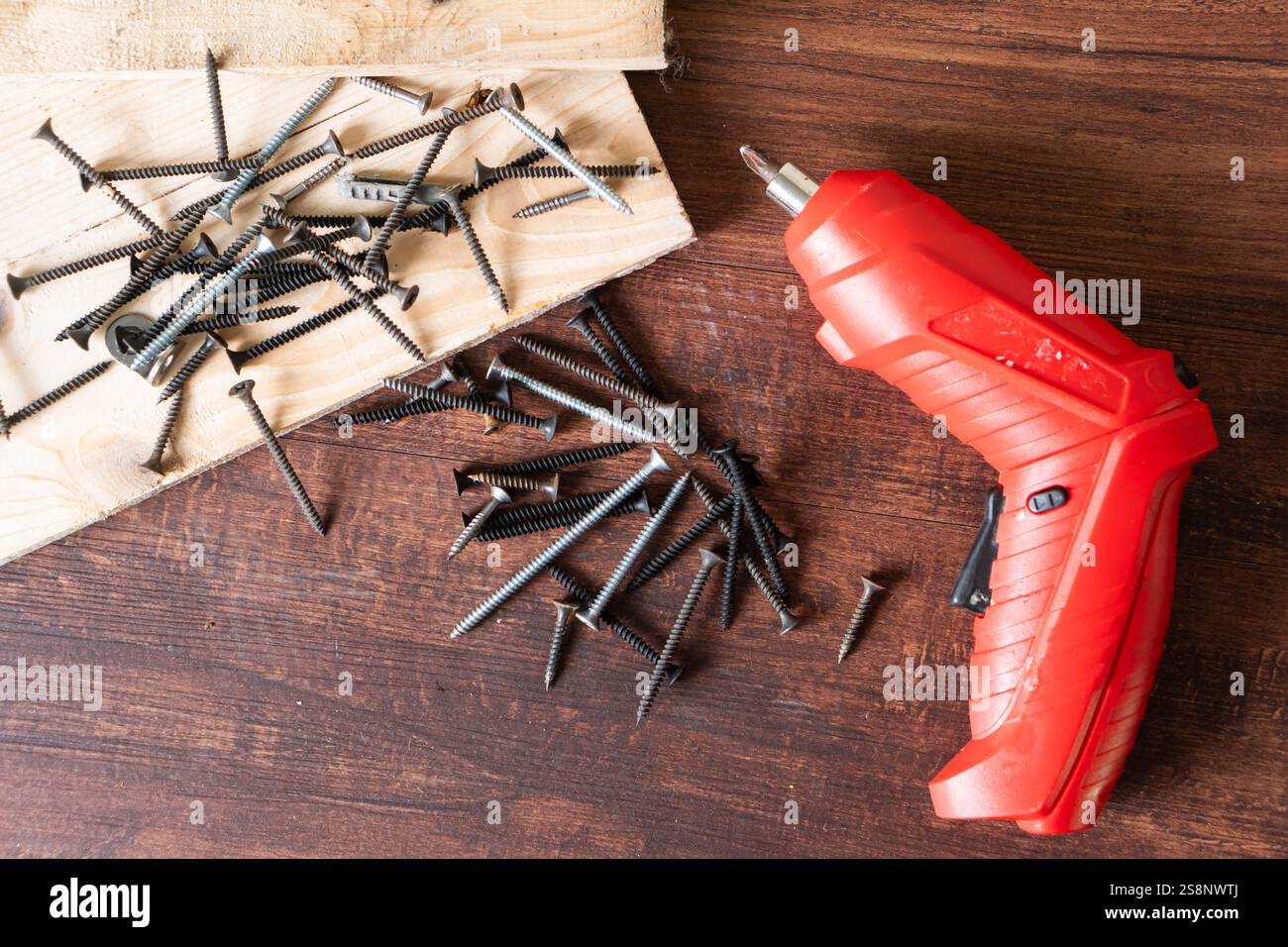 A collection of screws scattered on a wooden surface next to a red ...