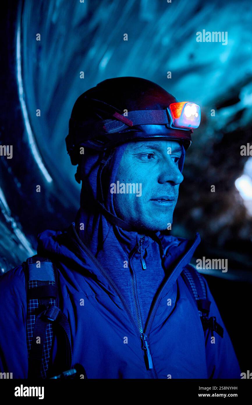 Alpinist climber in red helmet with glow headlamp in deep dark glacial ...