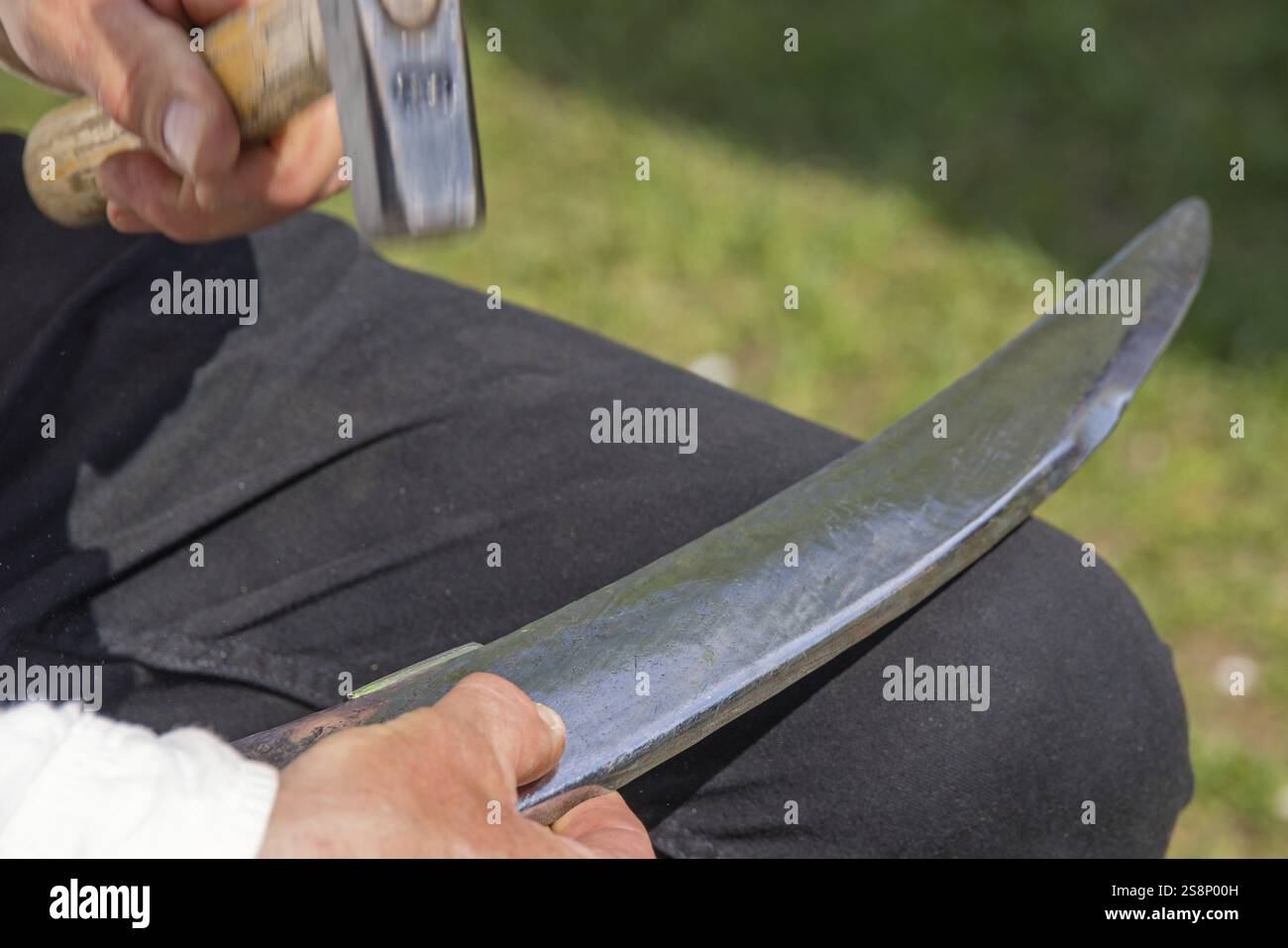 Man peening a scythe blade to sharpen it with a hammer, Sweden, Europe ...