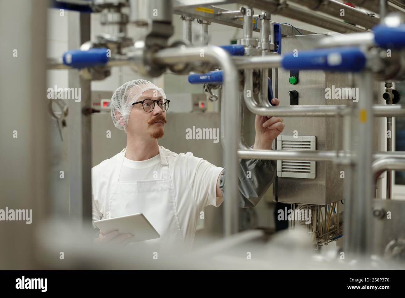 Man examining industrial machinery in food processing plant wearing ... Man examining industrial machinery in food processing plant wearing ...