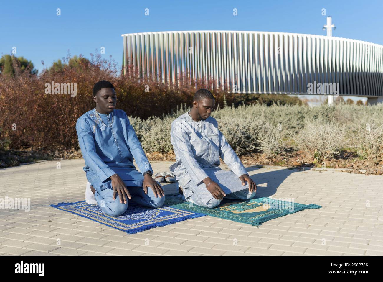 Two young senegalese men are kneeling on prayer rugs, performing salat ...