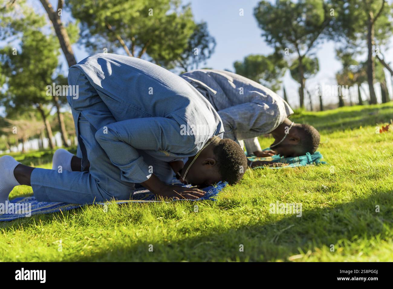 Three senegalese muslim men are kneeling on prayer rugs in a park ...