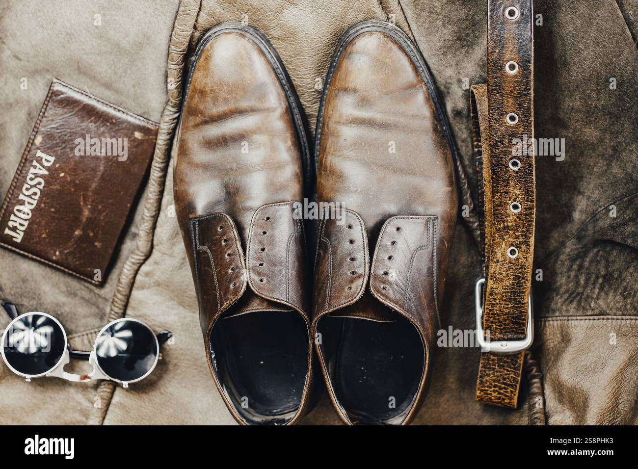 Brown leather shoes with a belt, passport, and sunglasses, creating a ...