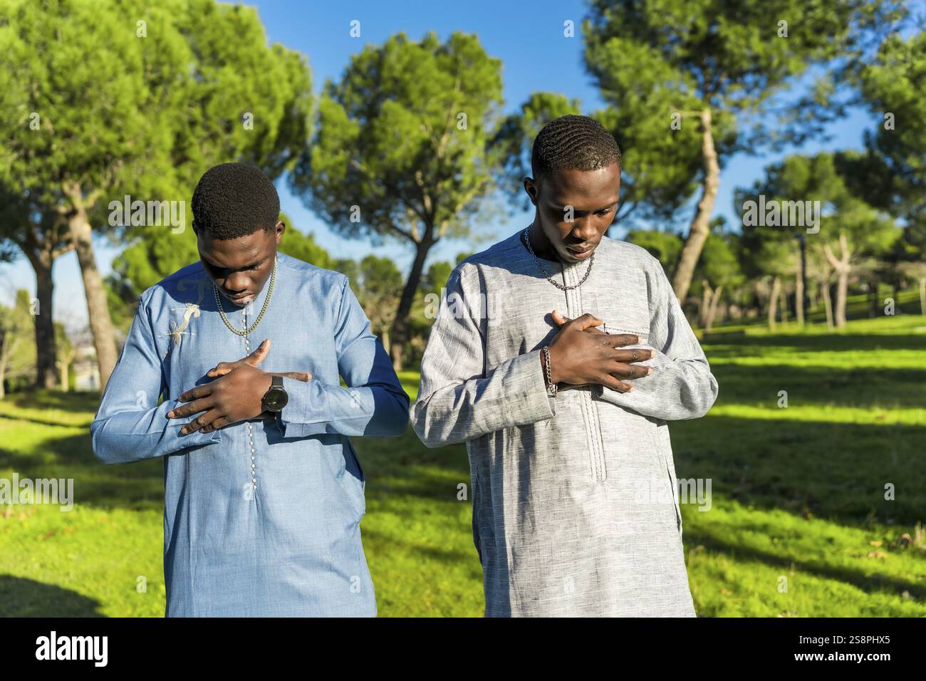 Two young senegalese men are praying outdoors in a park, wearing ...