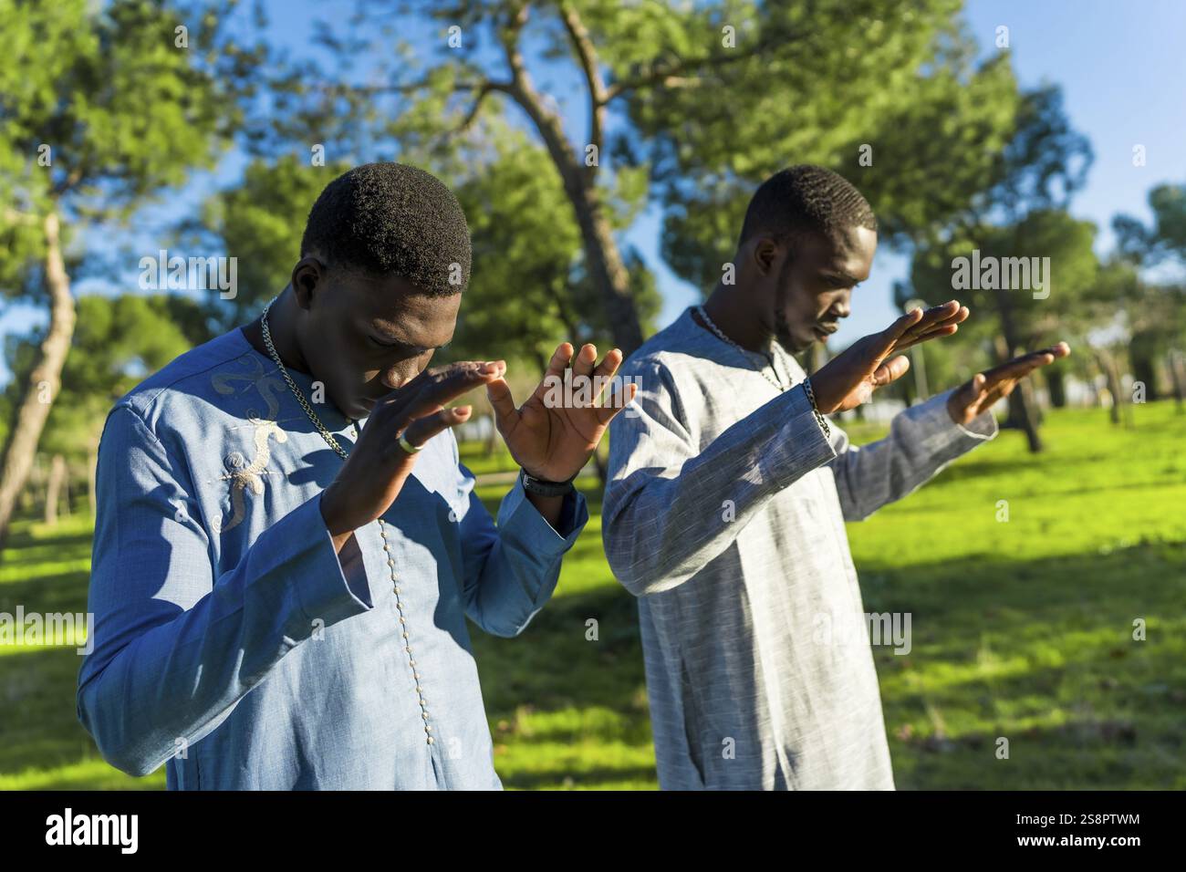 Two young senegalese men wearing traditional clothing are praying ...