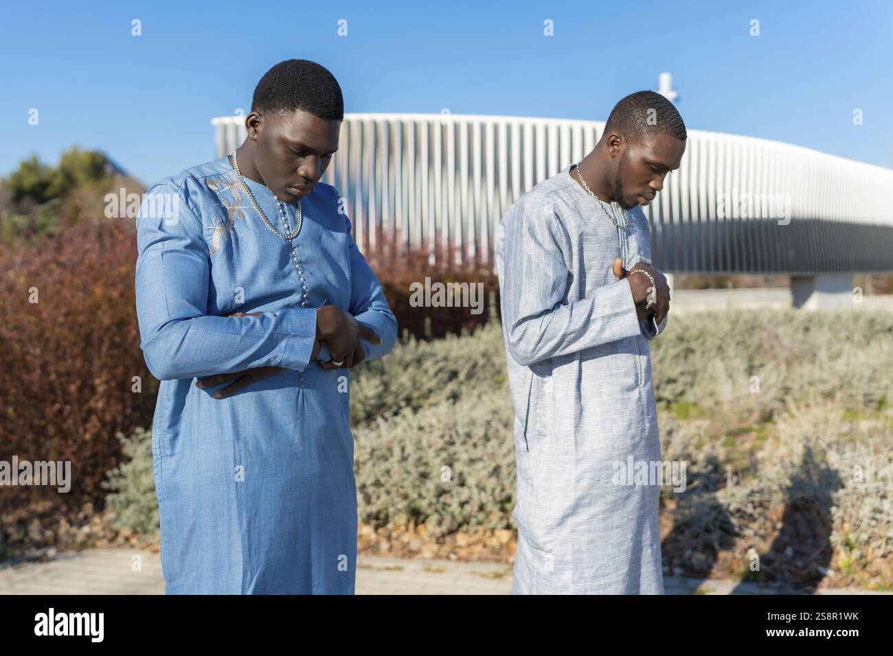Two young african muslim men wearing traditional dashiki clothing are praying outdoors ...