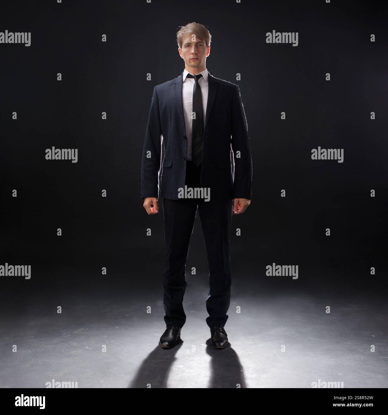In a dark studio, a man stands confidently in a crisp black suit and ...