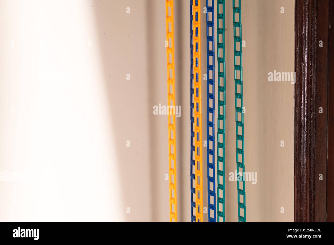 Colorful plastic chains hanging against a wall, with sunlight casting ...
