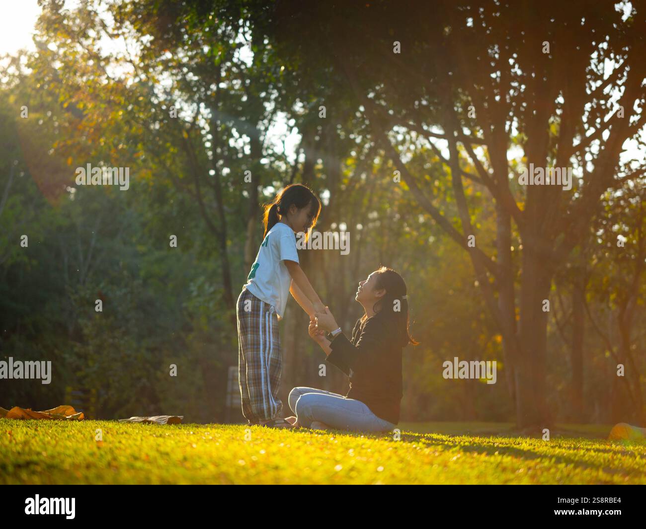 Mother and daughter are playing together in the park. Happy mother hugging her daughter sitting ...