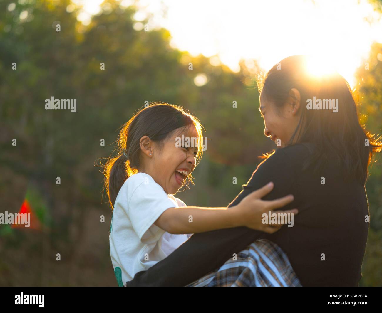 Mother and daughter are playing together in the park. Happy mother hugging her daughter sitting ...