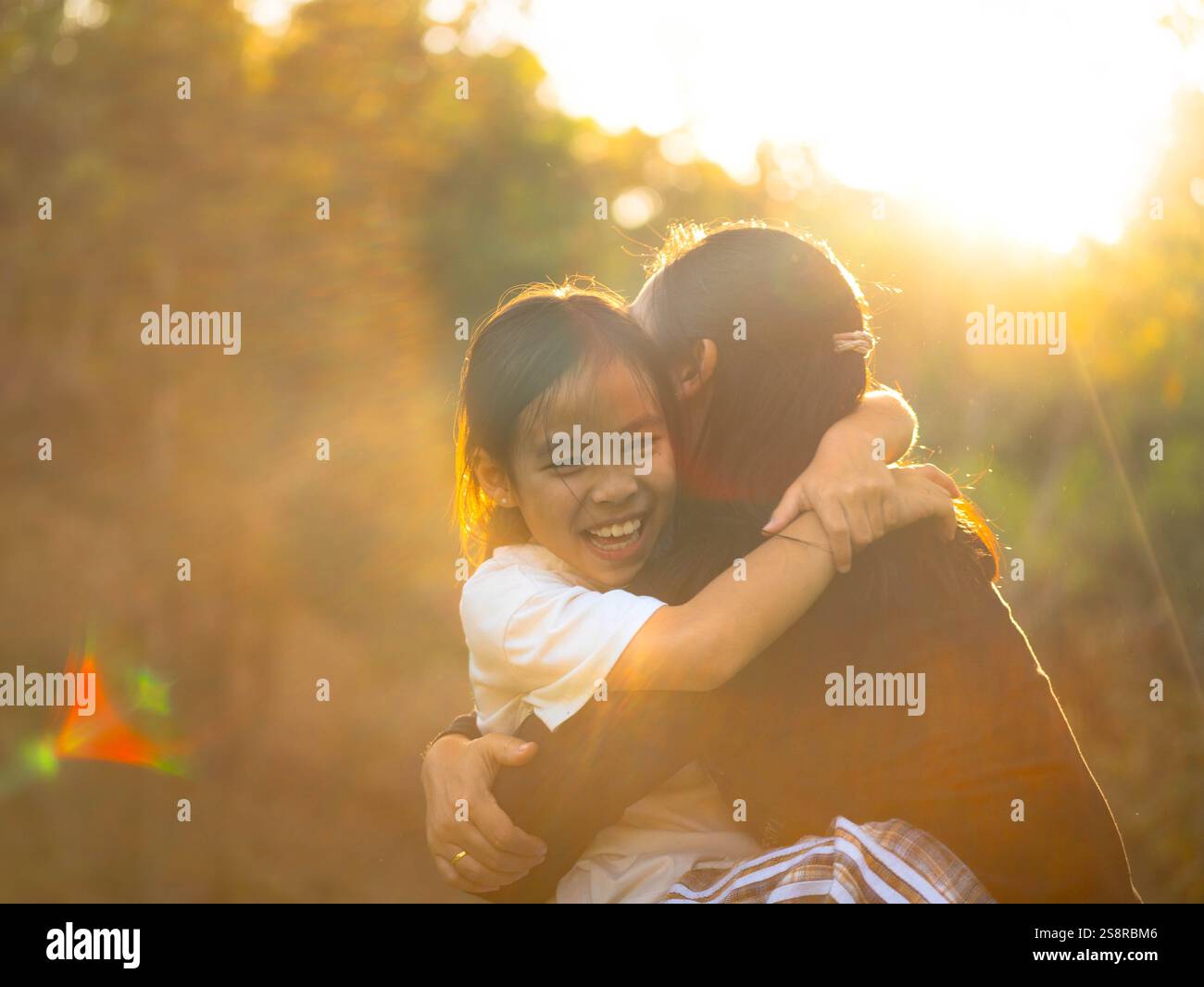 Mother and daughter are playing together in the park. Happy mother hugging her daughter sitting ...