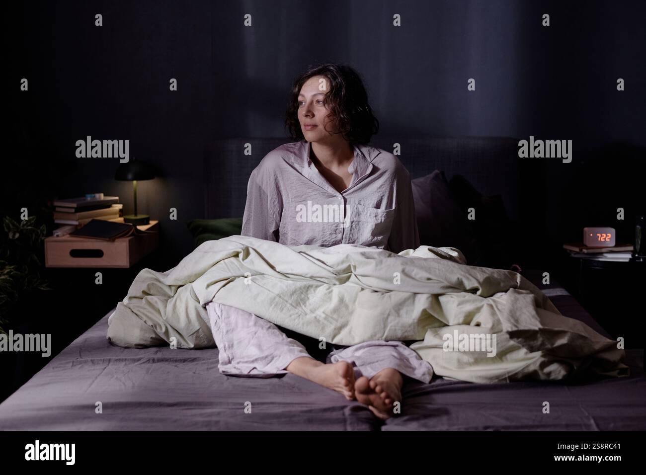 Smiling refreshed woman in comfy pajamas sitting in bed with olive ...