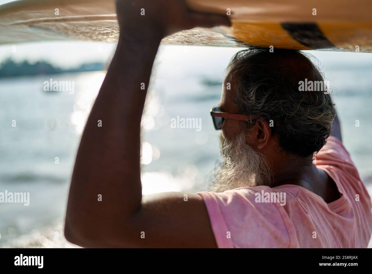 Senior man with surfboard walk along ocean shore. Elderly surfer enjoys ...