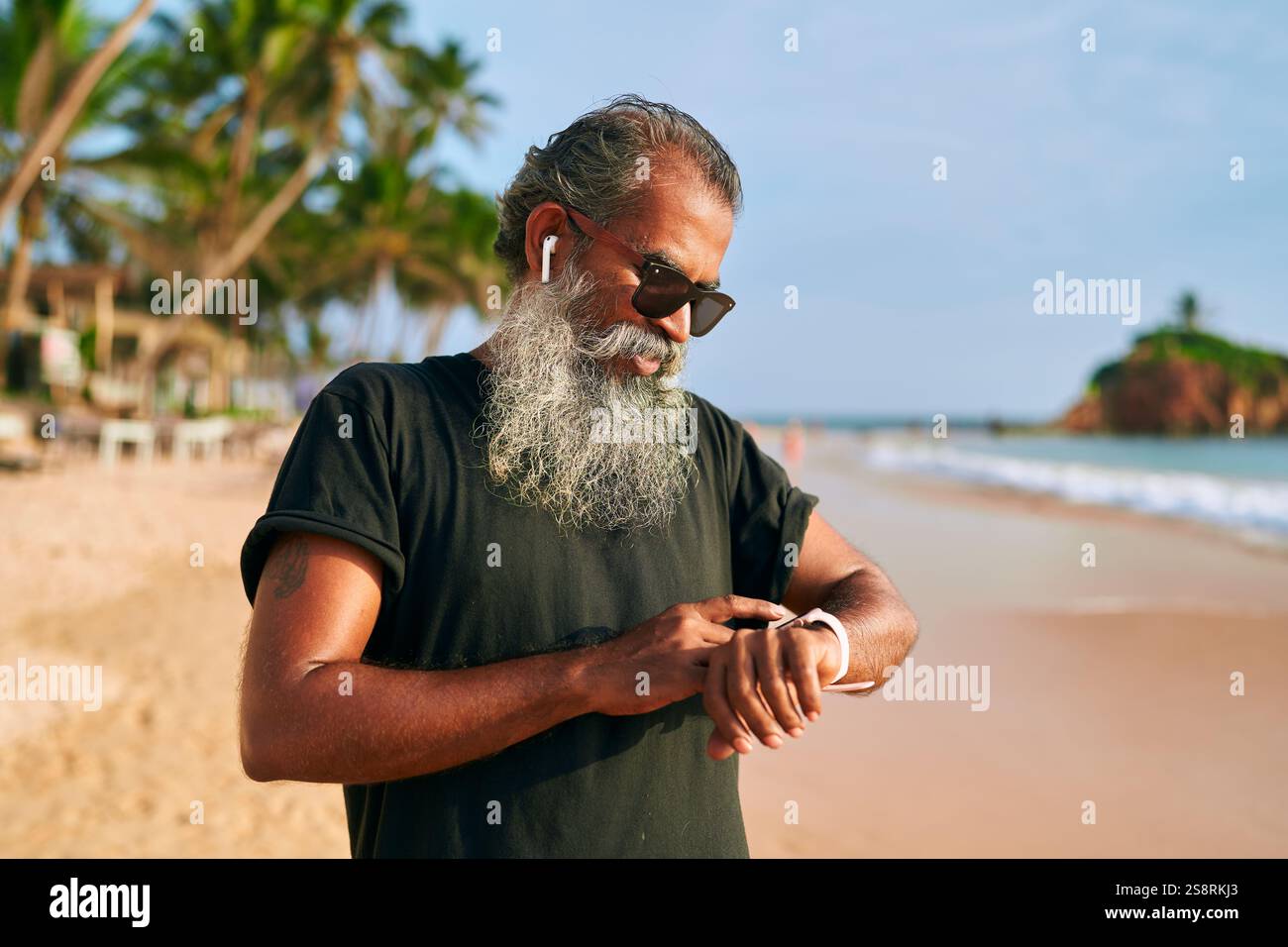 Stylish senior man with gray beard at beach uses smart watch. Wearing ...