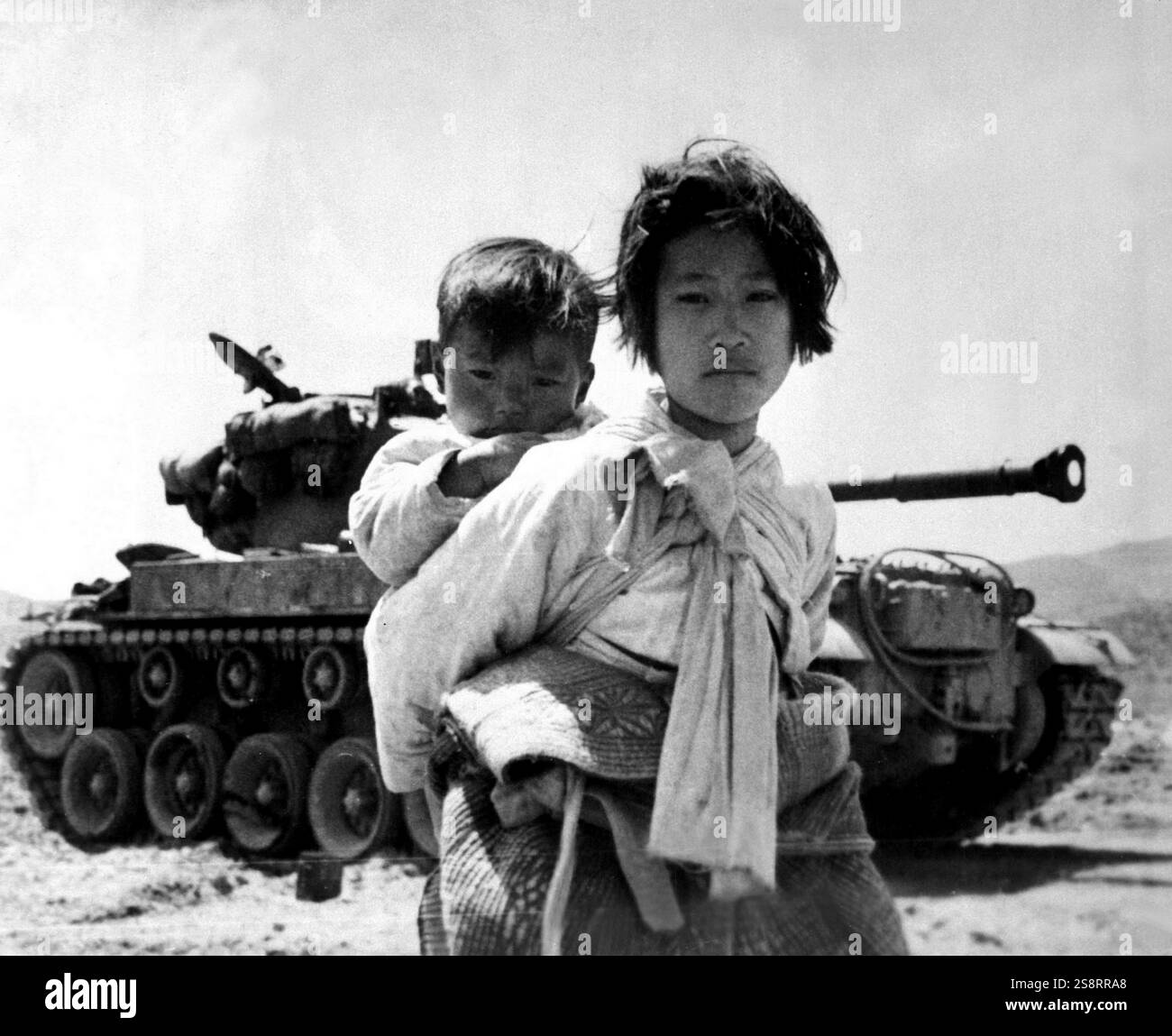 With her brother on her back a war weary Korean girl tiredly trudges by ...