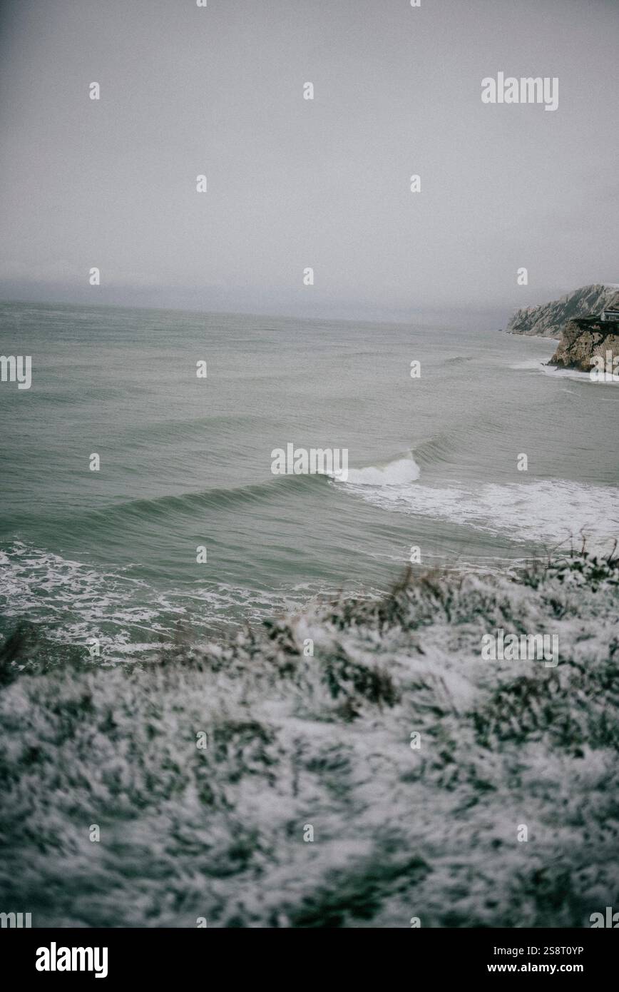 A snowy beach with a large wave crashing into the shore. The water is a ...