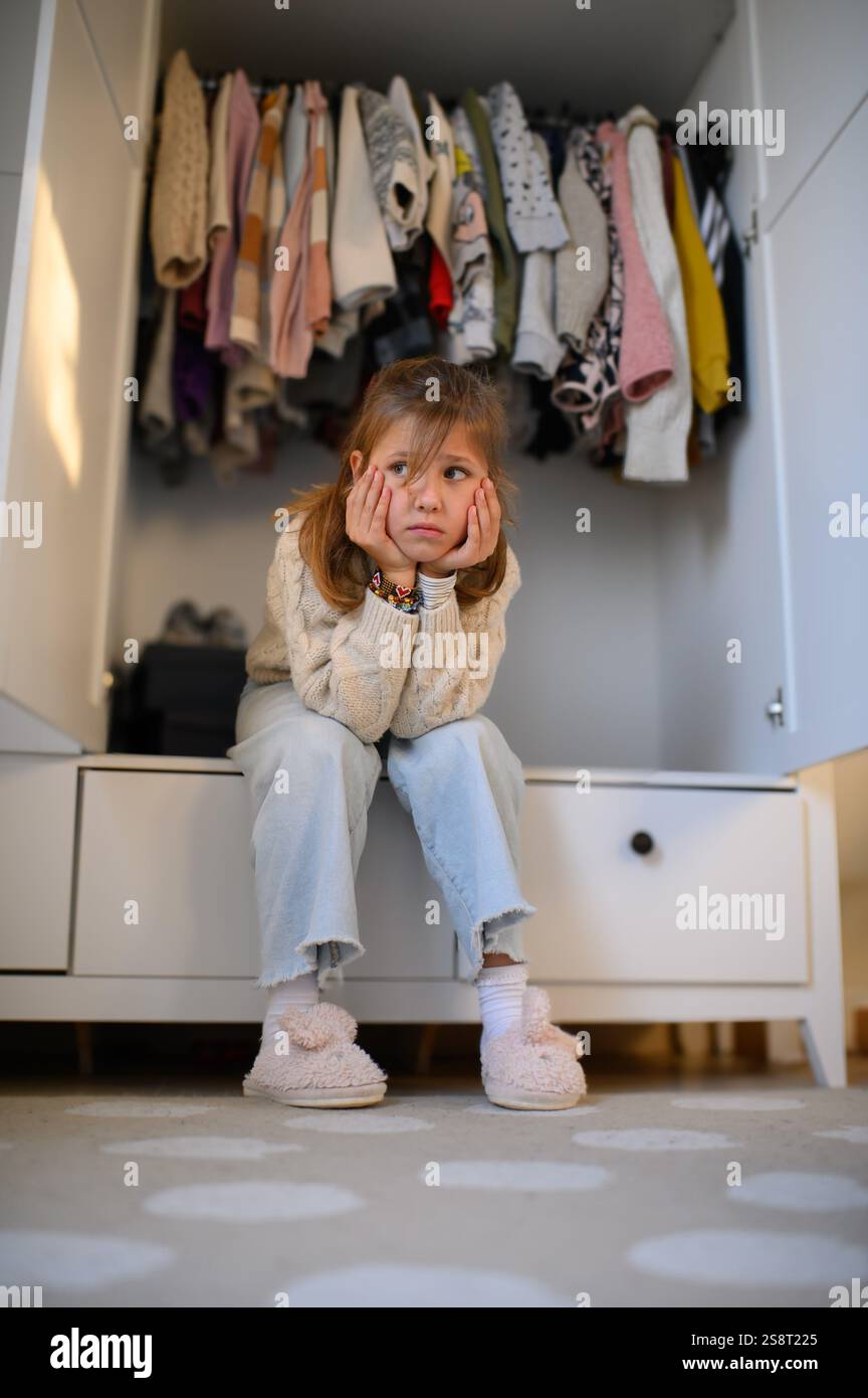 Girl is sitting close to her wardrobe with sad face and thinking what ...