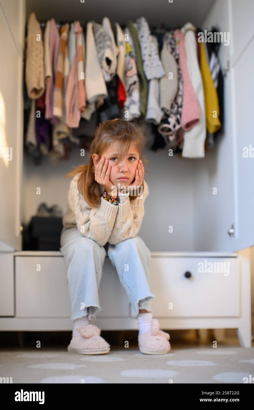 Girl is sitting close to her wardrobe with sad face and thinking what ...
