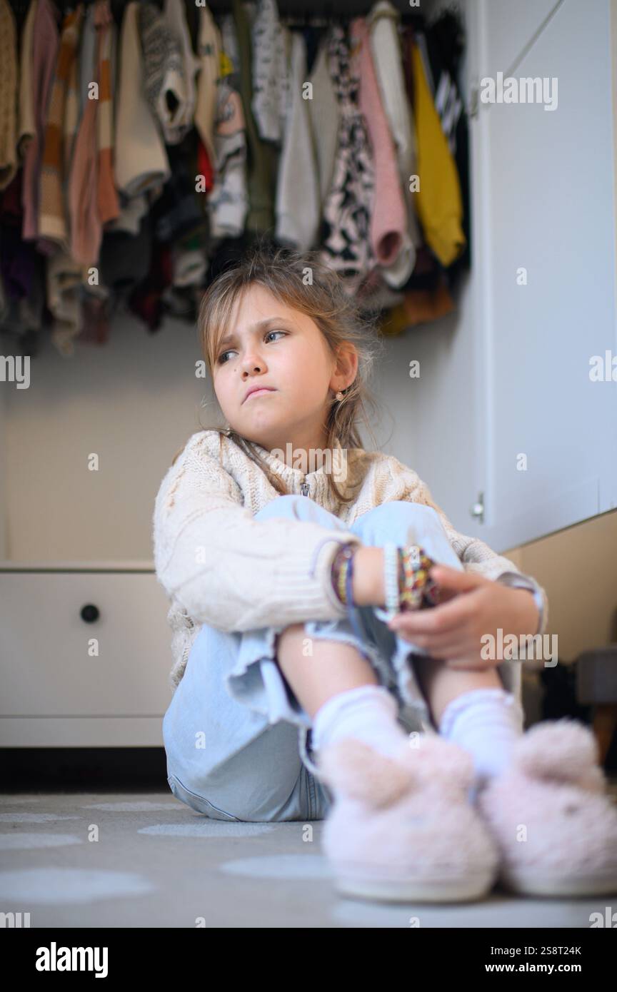 Girl is sitting close to her wardrobe with sad face and thinking what ...