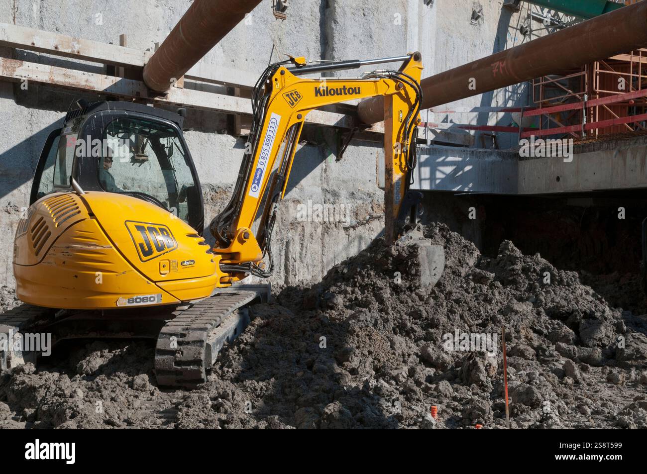 A JCB mini excavator digs the ground. Two large metal beams ensure the ...