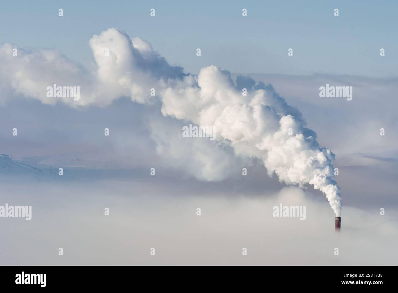 Thick smoke billowing from a tall chimney above low-lying clouds in a ...