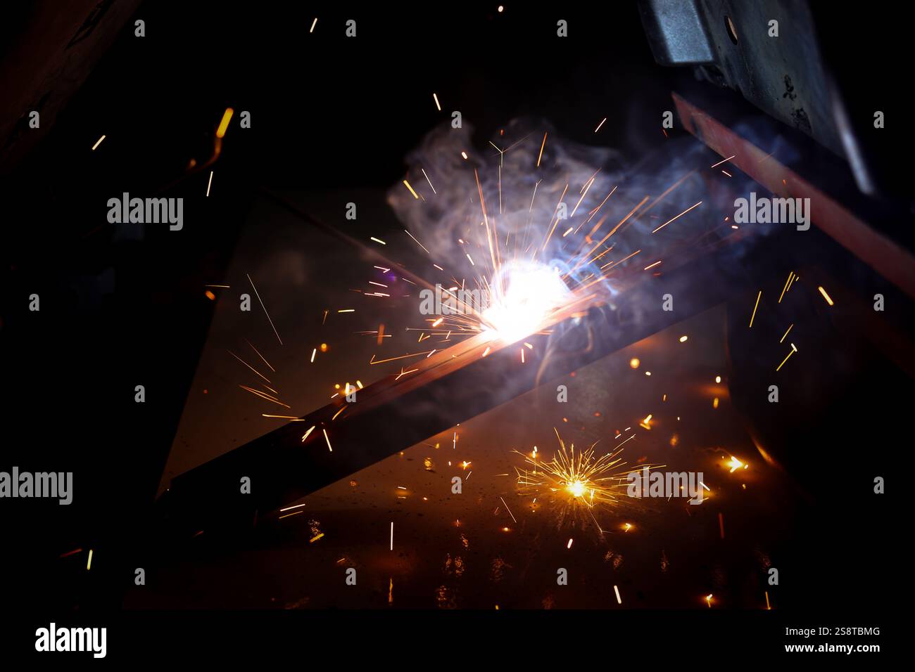 Welding sparks flying from metal as worker fuses steel with intense ...