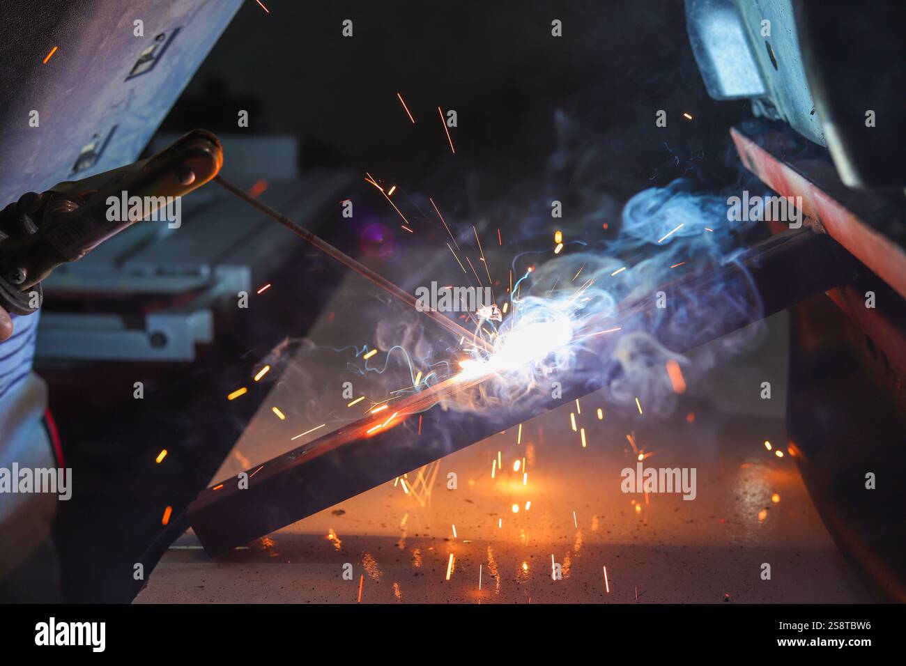 Welding sparks flying from metal as worker fuses steel with intense ...