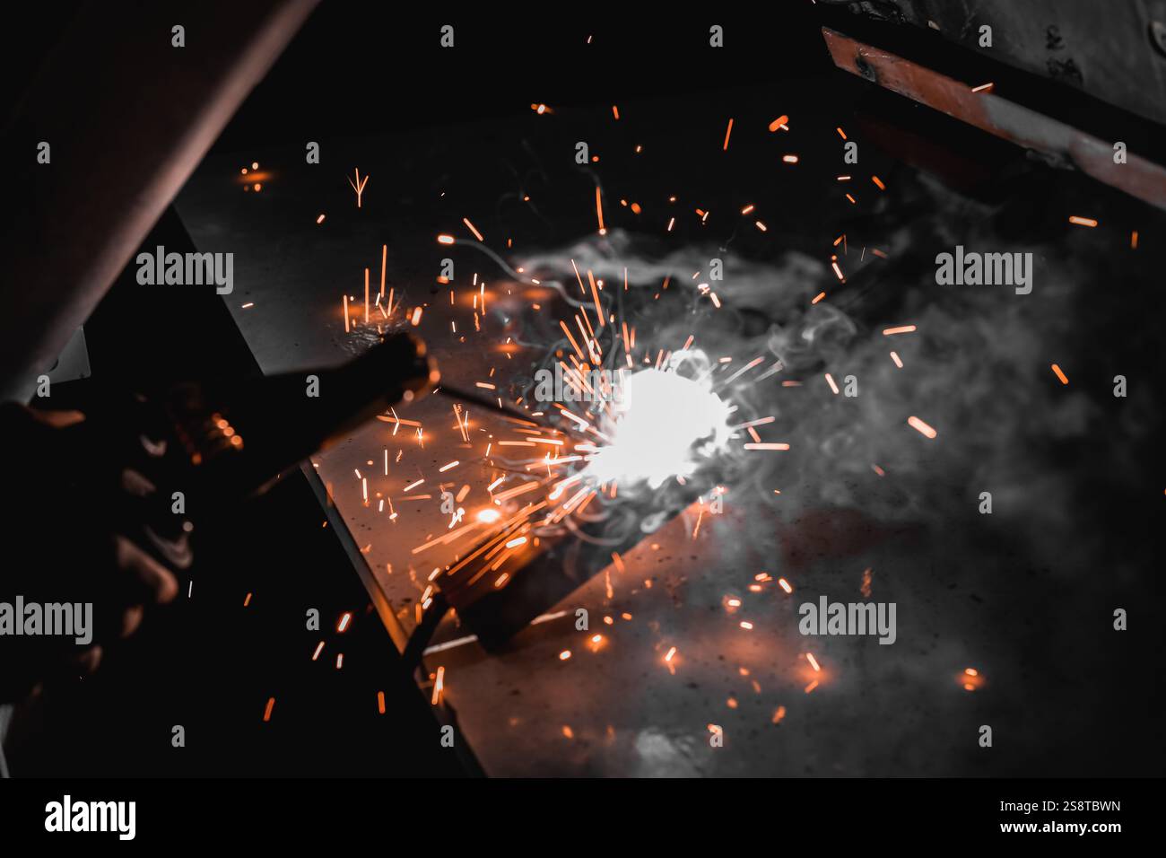 Welding sparks flying from metal as worker fuses steel with intense ...