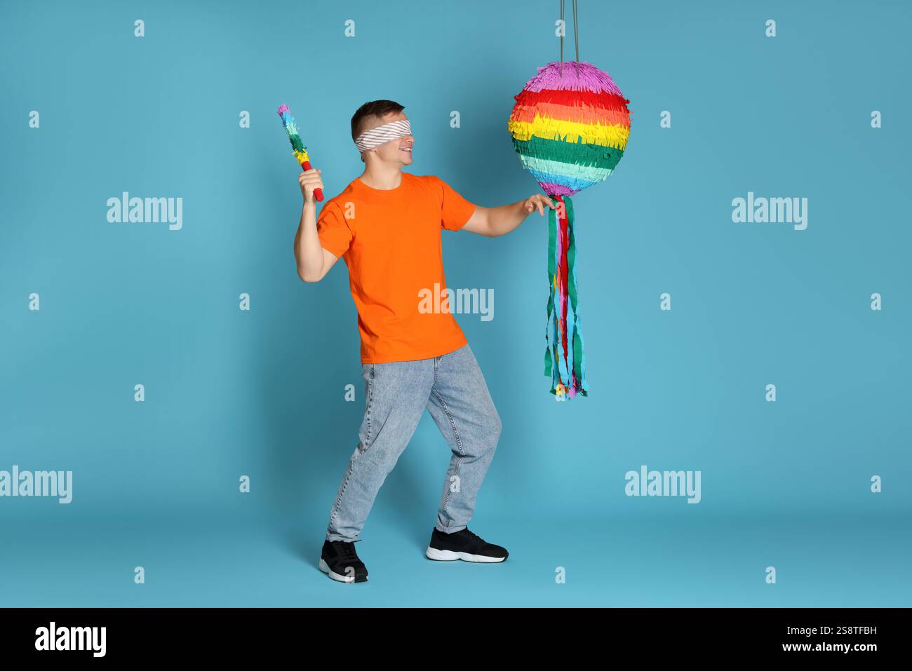 Man with tied eyes breaking pinata on light blue background Stock Photo ...
