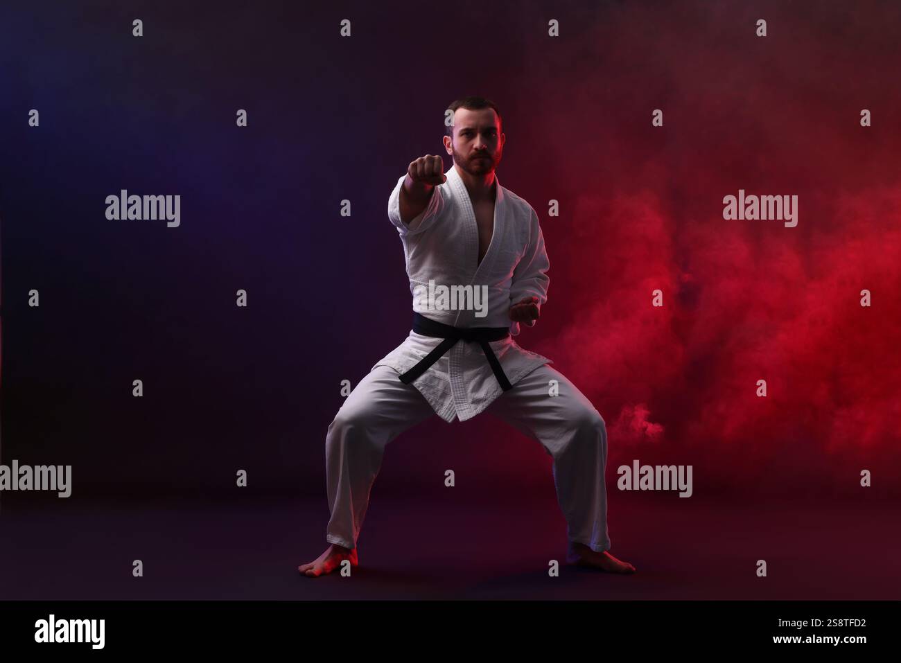 Man wearing uniform practicing karate in color lights and smoke against ...