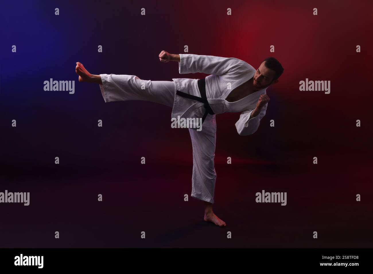 Man wearing uniform practicing karate in color lights against black ...