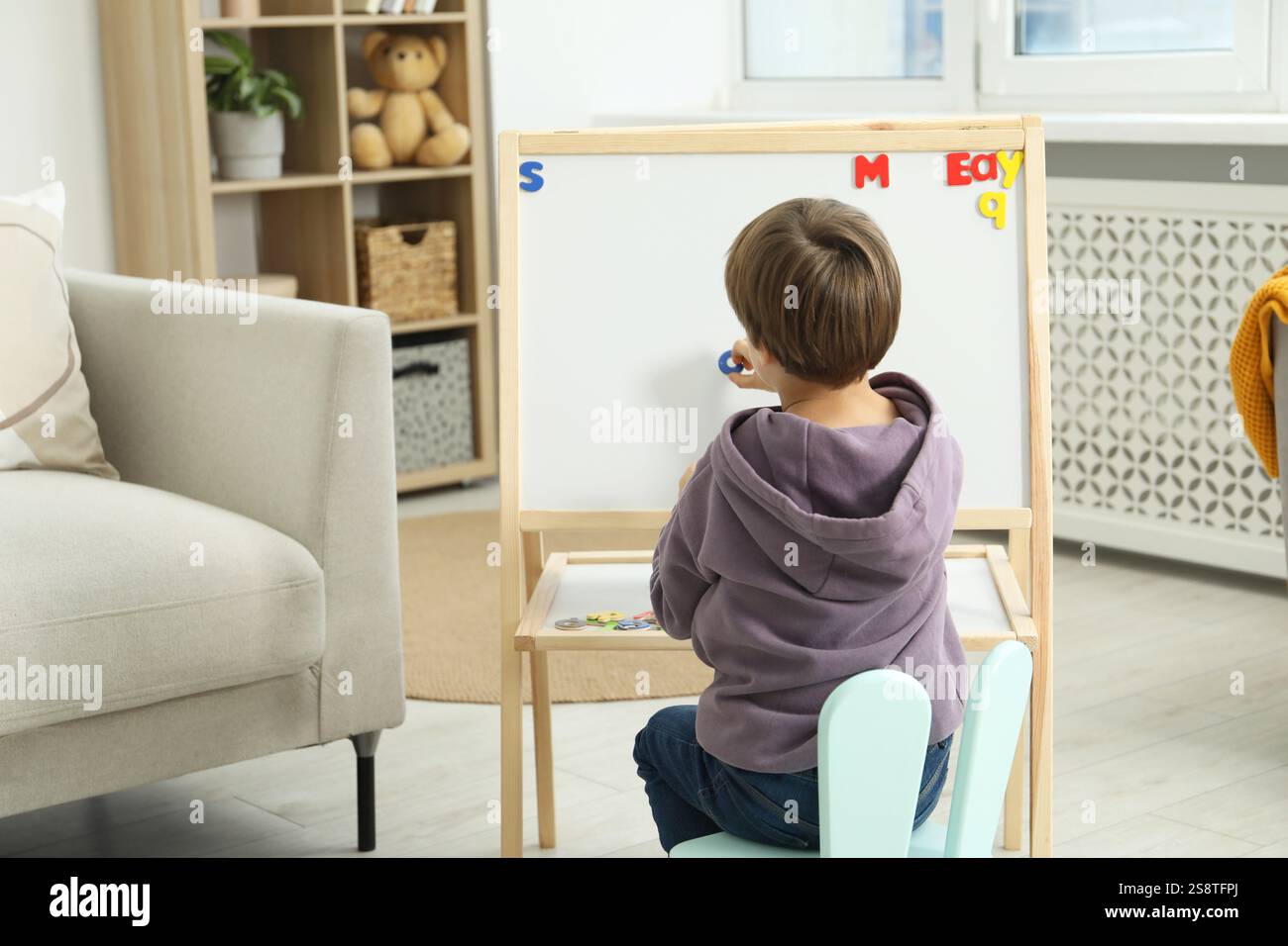 Little boy learning alphabet with magnetic letters indoors, back view ...
