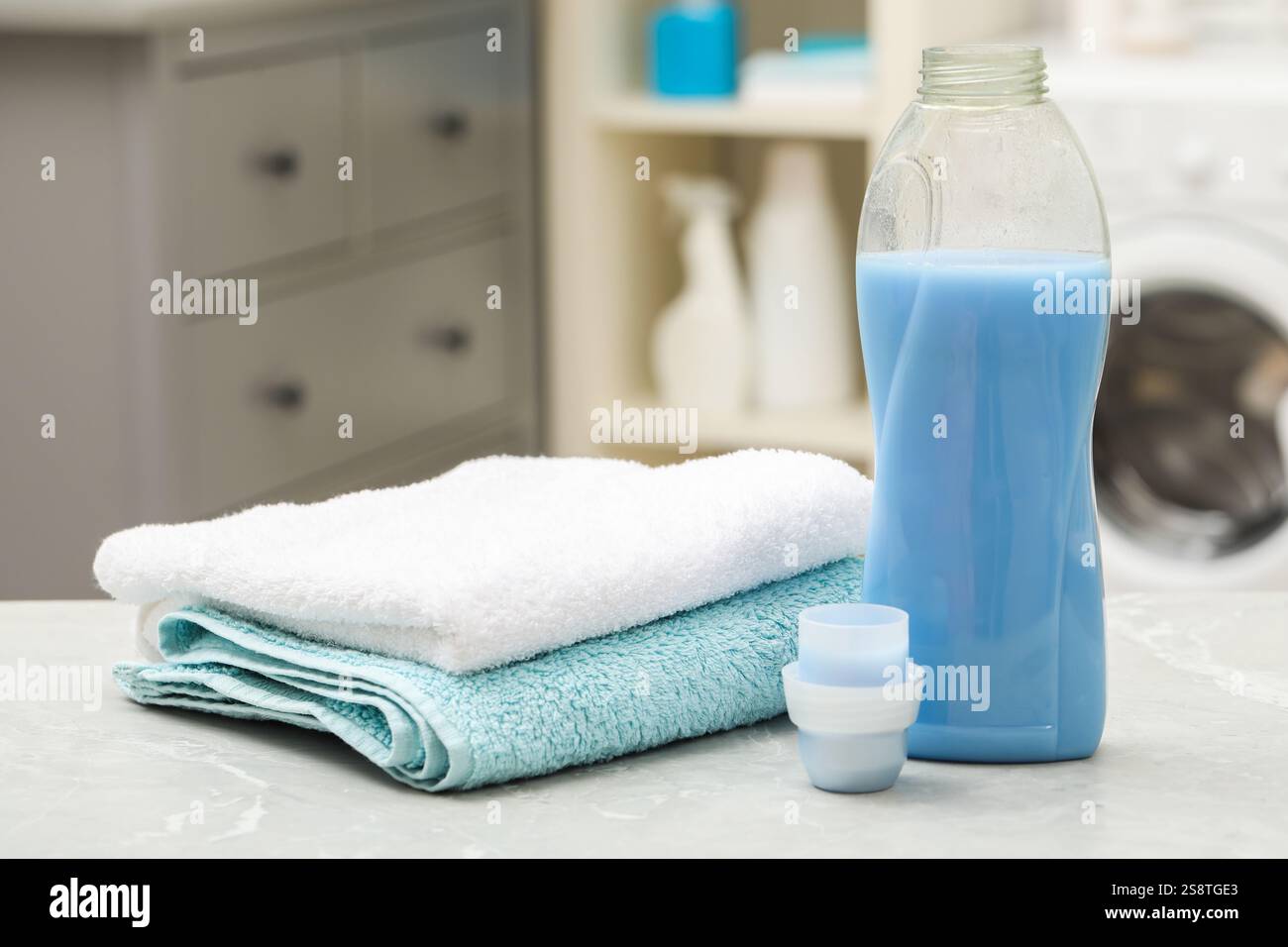 Laundry detergent and clean terry towels on light grey marble table in ...