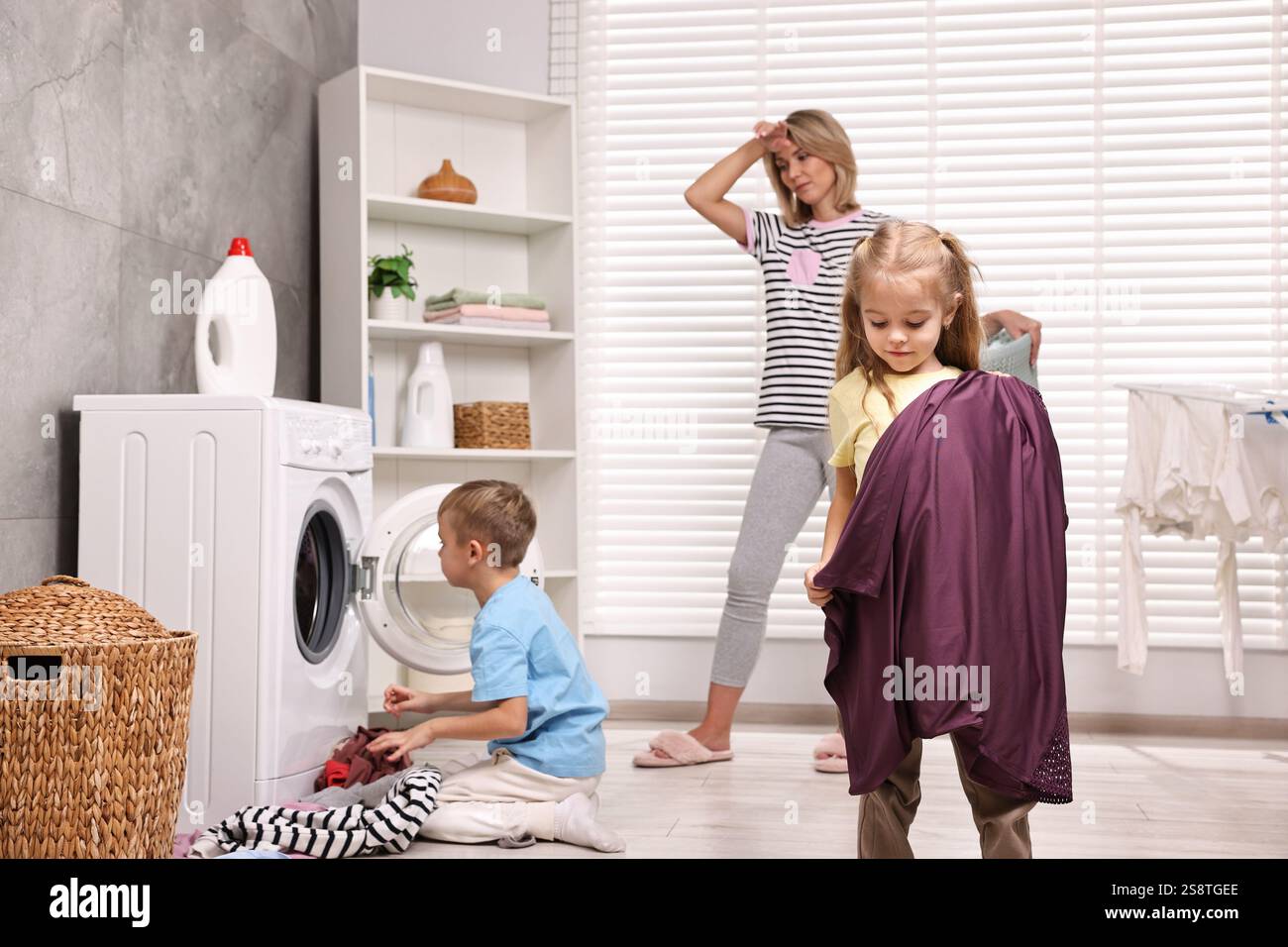 Tired housewife and her kids doing laundry together in bathroom Stock Photo - Alamy