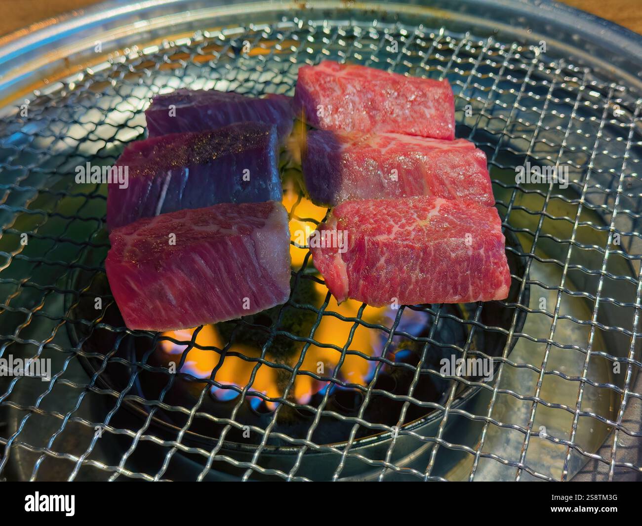 Close up of raw beef meat being cooked on wire grill with natural gas ...